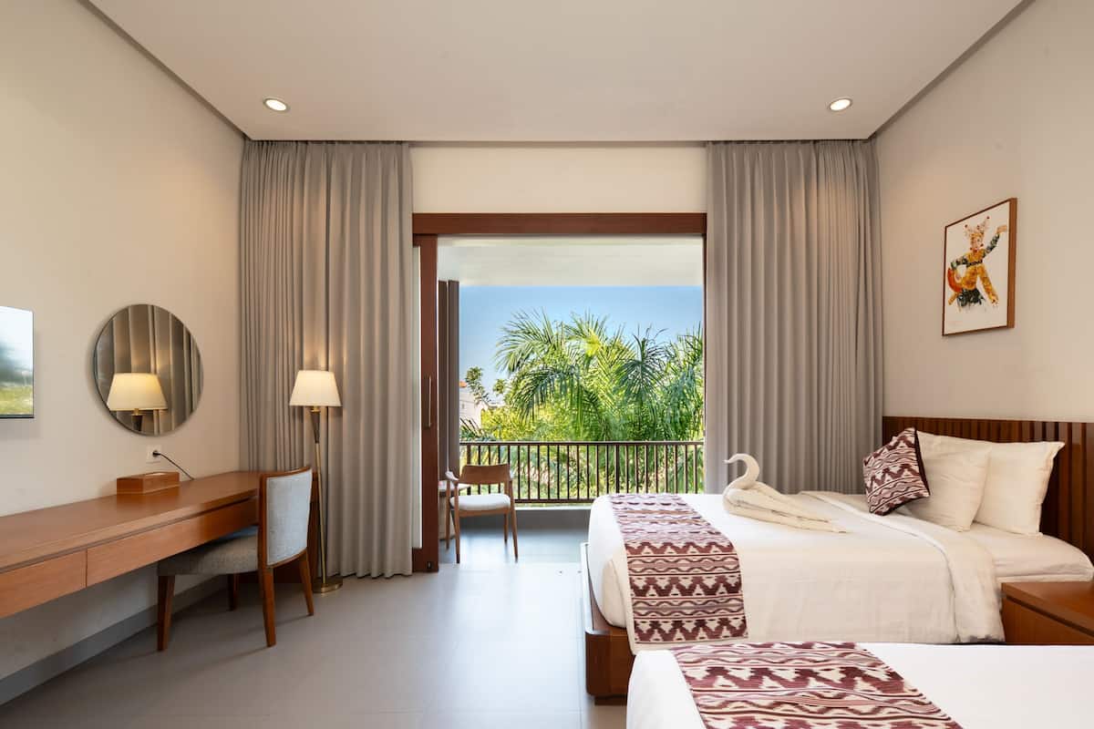 Quarto de hotel com cama, escrivaninha, cadeira e varanda com vista para o verde.