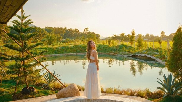 Uma pessoa parada perto de uma piscina, com vista para um lago e vegetação.