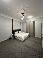 Quarto de hotel moderno com uma cama grande, uma mesa de cabeceira, uma obra de arte na parede e um teto com design geométrico.