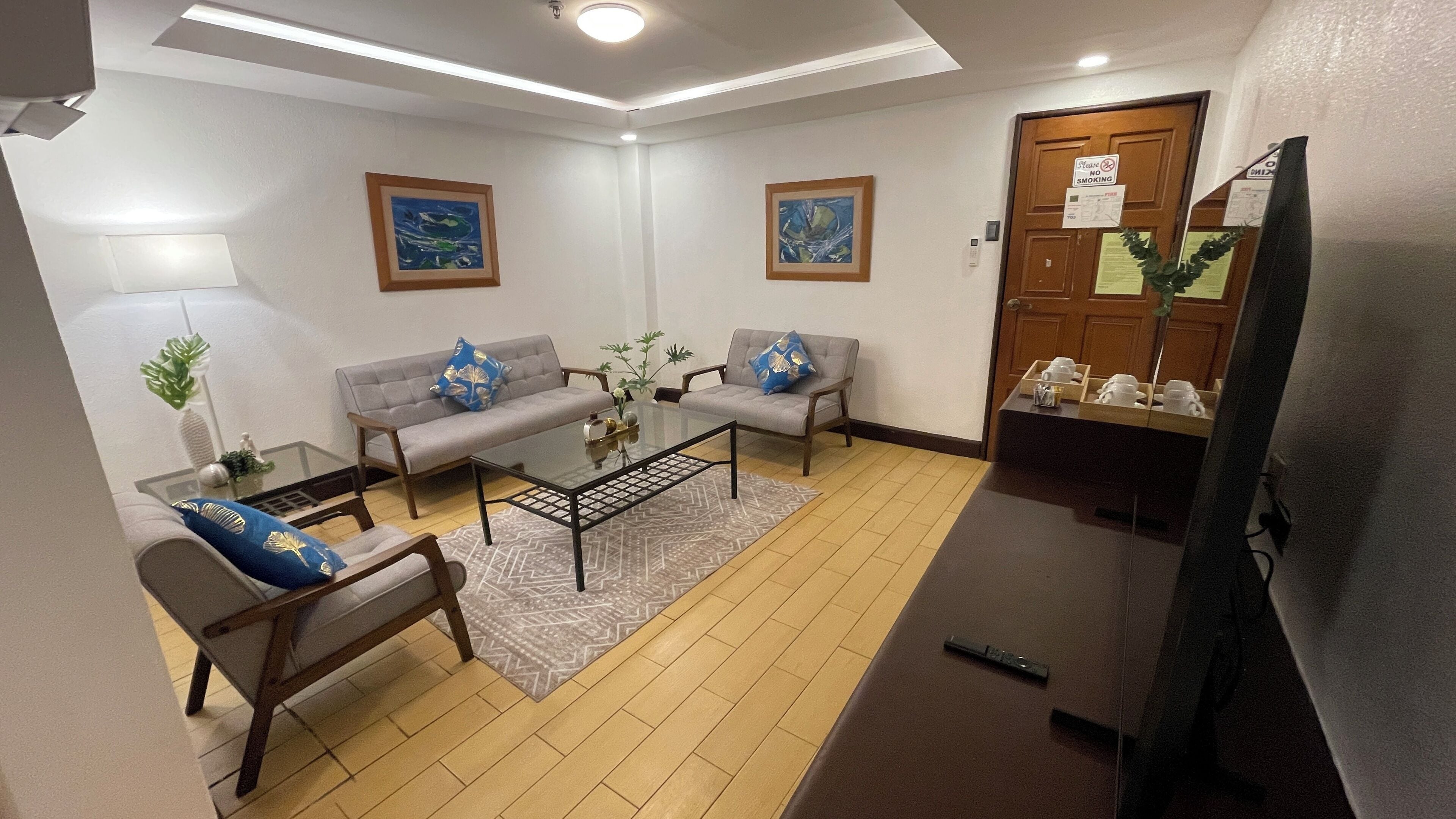 Sala de estar com dois sofás, uma mesa de centro e uma televisão. Existem duas pinturas emolduradas nas paredes.