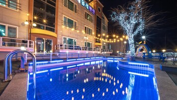 Hotel com piscina, área externa com mesas e cadeiras, e luzes decorativas.