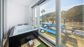 Um banheiro moderno com chuveiro em vidro, banheira e vista para área externa com mesa de piquenique e decoração de arco-íris.