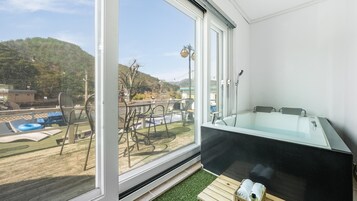 Varanda com hidromassagem envidraçada, área de estar externa e vista para uma piscina e colinas.