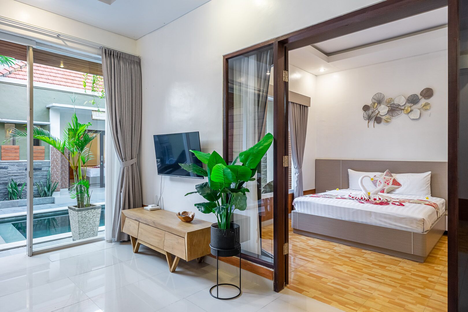 Quarto moderno com cama, televisão, escrivaninha de madeira e uma janela grande com cortinas.