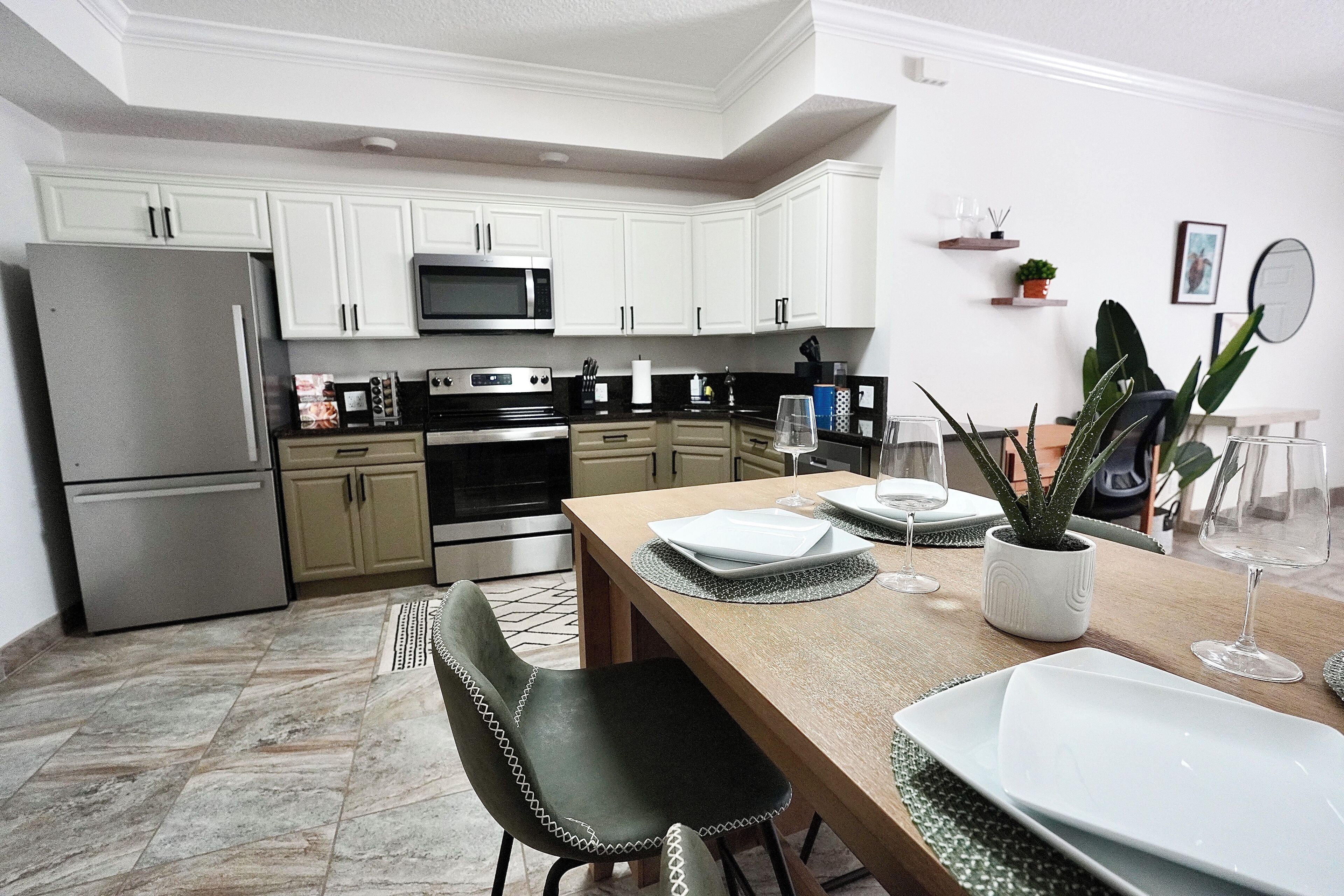 Uma cozinha moderna com armários brancos, eletrodomésticos de aço inoxidável e uma mesa de jantar de madeira para dois.
