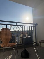Uma varanda com cadeiras de vime, uma mesa com xícaras e um guarda-corpo de metal decorativo.