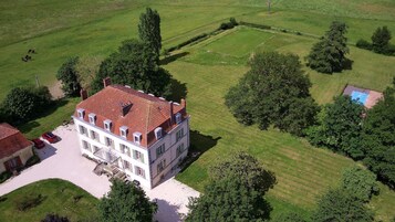 Um edifício grande, de vários andares, com telhado de telhas vermelhas, cercado por campos verdes exuberantes e árvores.