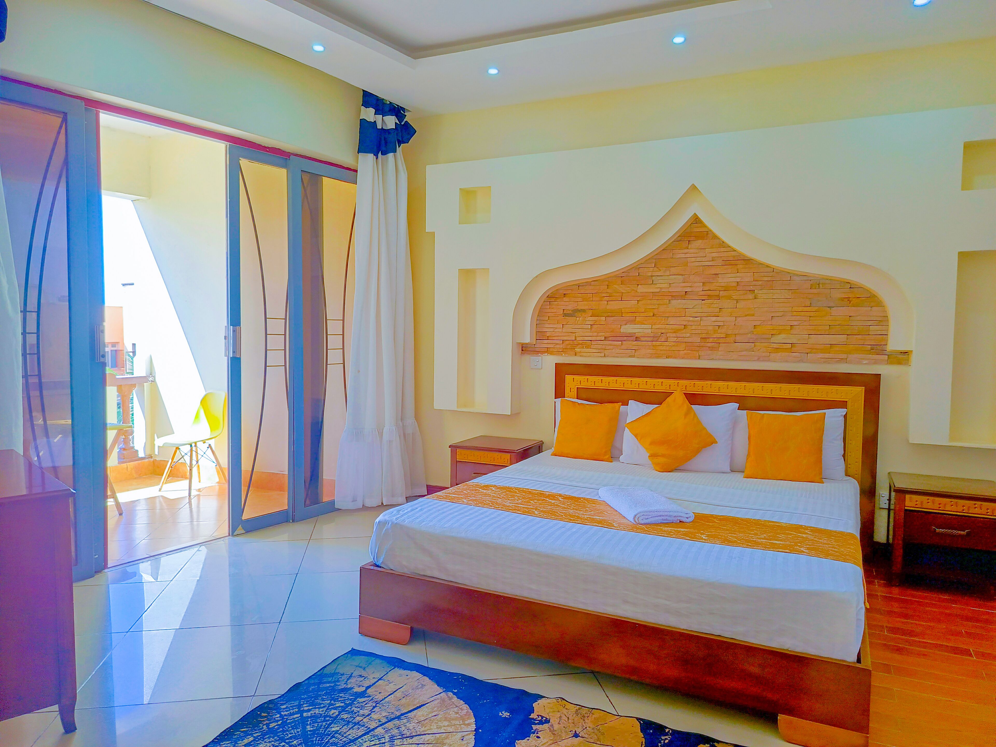 Quarto com cama grande, cabeceira de madeira e vista para uma varanda através de uma porta de vidro.