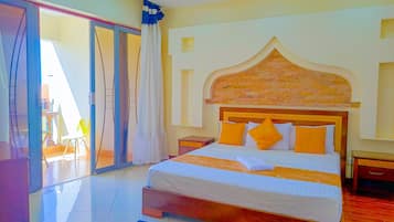 Quarto com cama grande, cabeceira de madeira e vista para uma varanda através de uma porta de vidro.