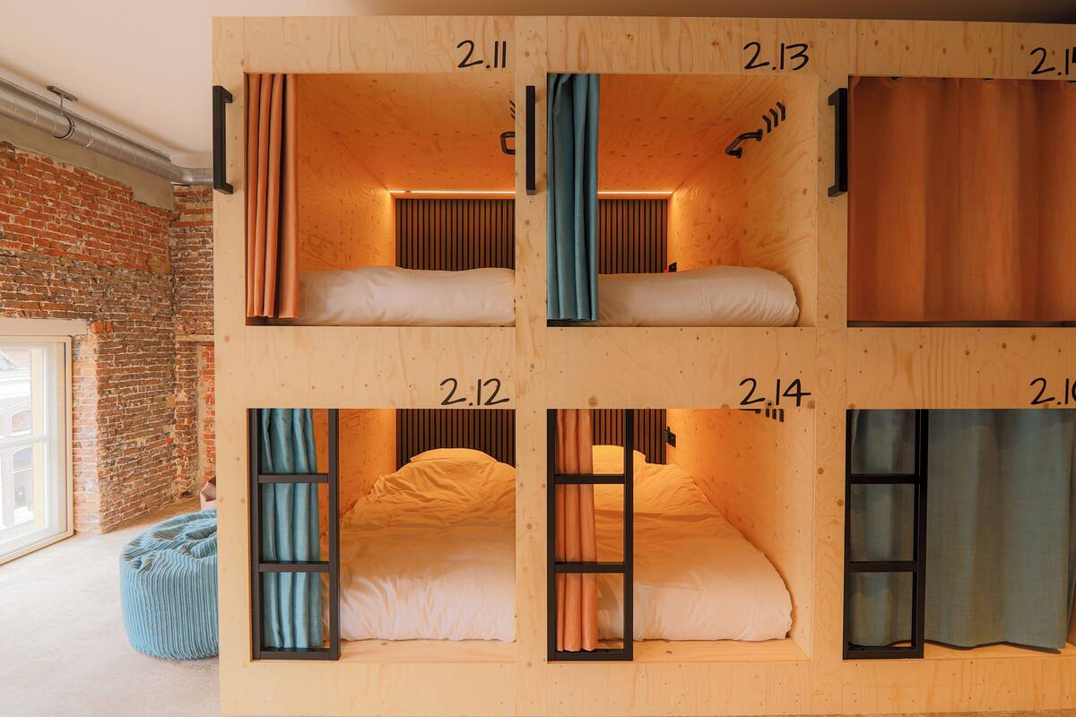 Quarto com quatro camas de madeira, cada uma com cortina e um número em cima.