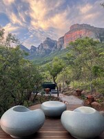 Um deck de madeira com três vasos de pedra, cercado por vegetação exuberante e montanhas ao fundo.