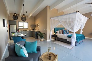 Quarto moderno com cama de dossel, área de estar com sofá e cozinha ao fundo.