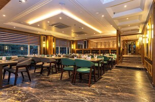 Um restaurante espaçoso com pé direito alto, piso de mármore e diversos tipos de assentos, incluindo cabines e mesas.