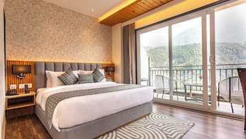 Quarto moderno com uma cama grande, cabeceira de madeira, mesa de cabeceira com abajur e vista para uma varanda com móveis.