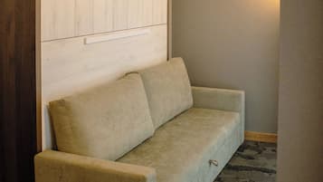 Um sofá em tons neutros com cabeceira de madeira, num quarto com carpete estampado e luminária fixada na parede.