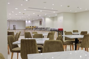 Restaurante com mesas de mármore e cadeiras estofadas, iluminação embutida no teto e um painel decorativo.