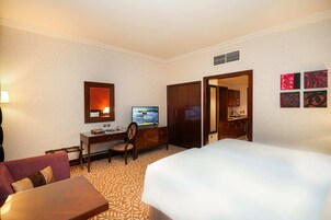 Quarto de hotel com cama, escrivaninha, cadeira e televisão.