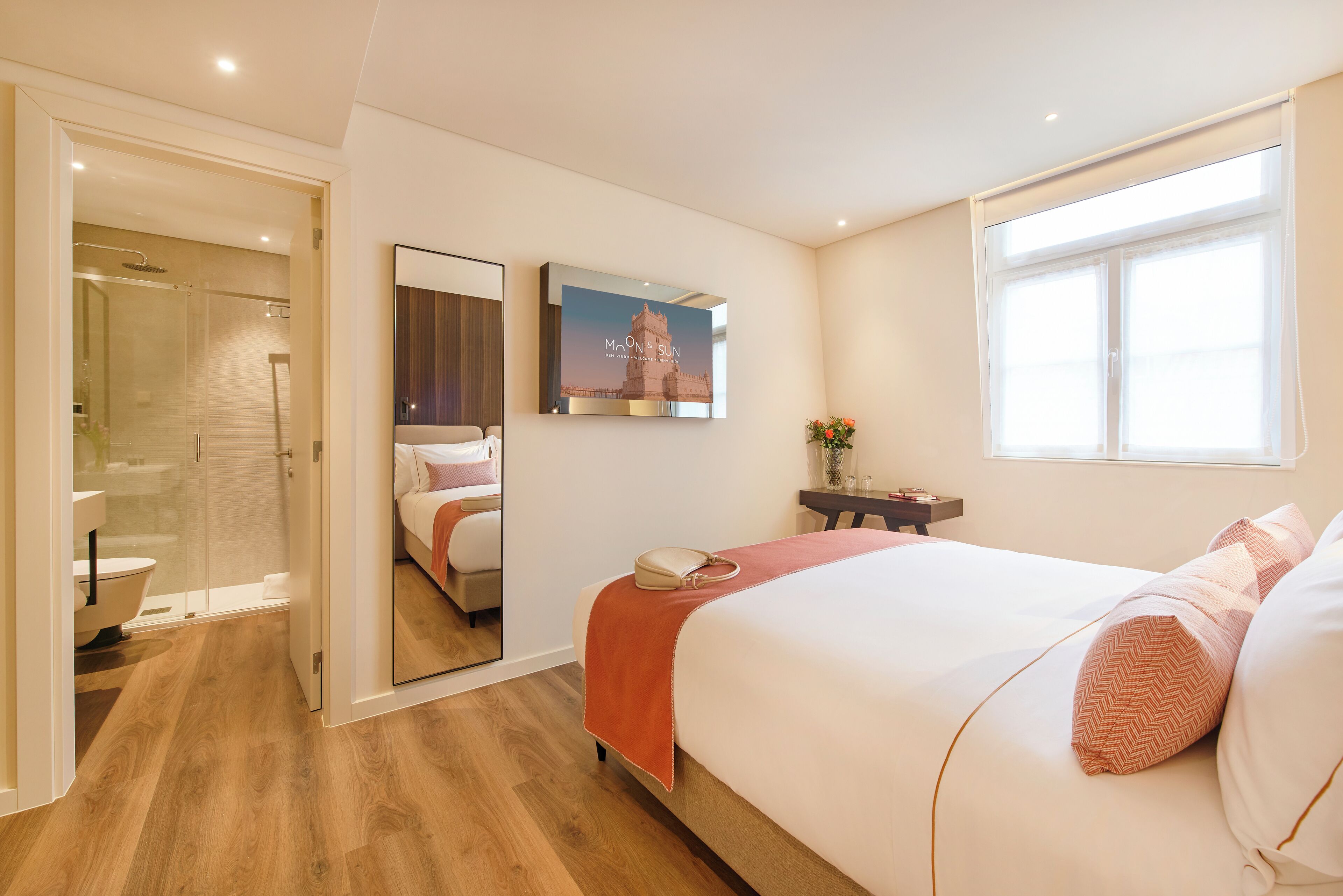 Quarto de hotel com cama, mesa de cabeceira, espelho, janela e área de chuveiro.
