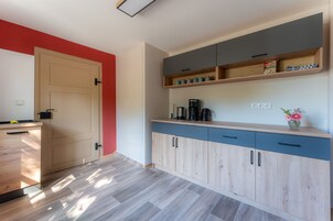 Cozinha moderna com armários de madeira clara, bancada cinza e uma parede com detalhes vermelhos.