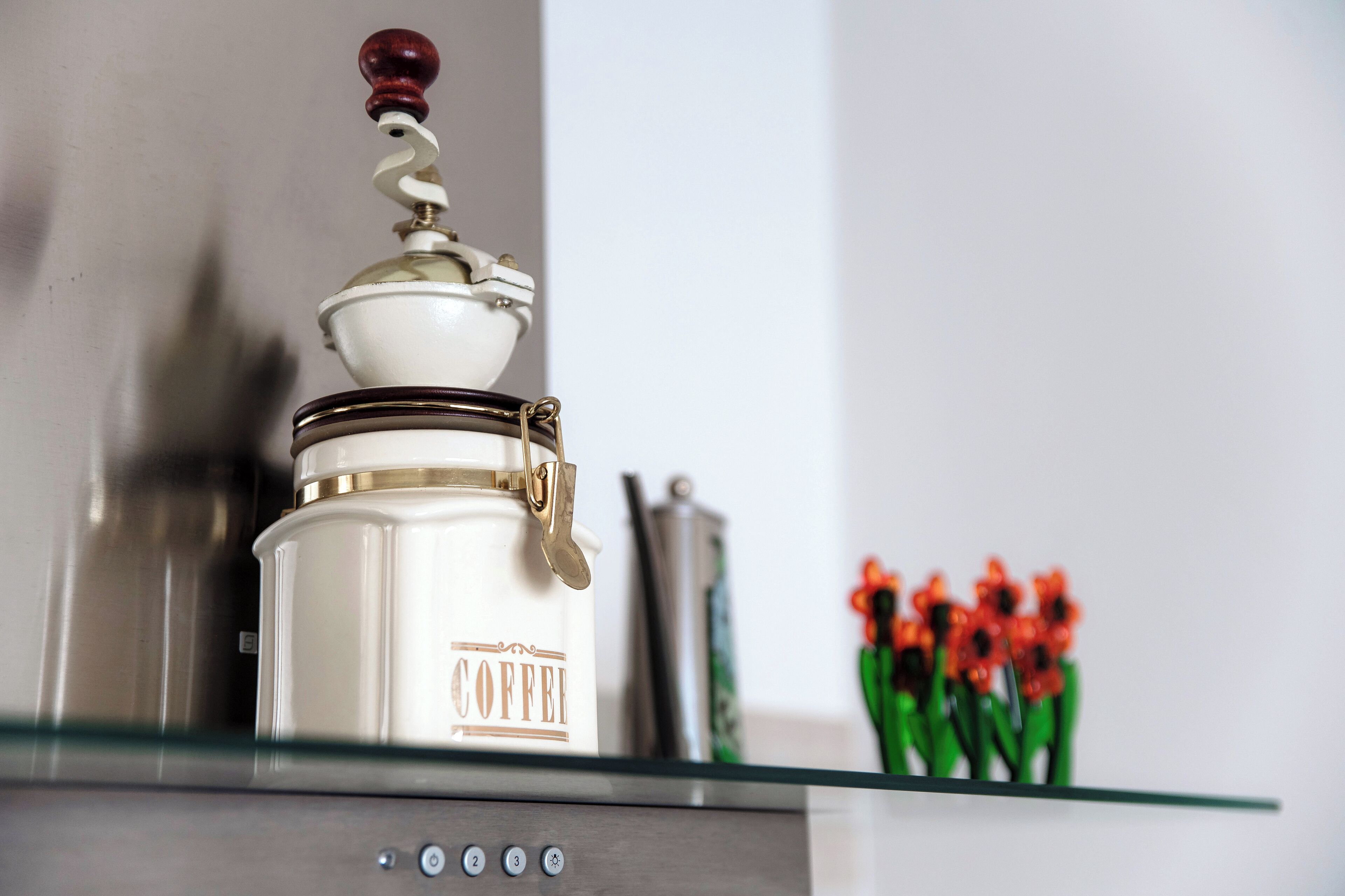 Uma cafeteira numa prateleira de vidro, com um eletrodoméstico ao fundo.