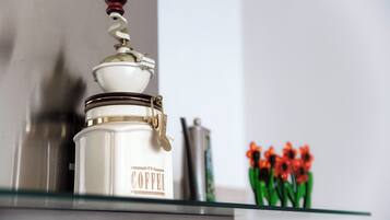 Uma cafeteira numa prateleira de vidro, com um eletrodoméstico ao fundo.