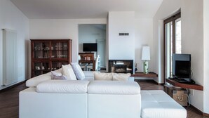 Uma sala de estar moderna com um sofá seccional branco, um armário de madeira, uma lareira e uma televisão.