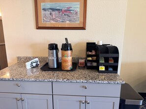Uma bancada de cozinha com cafeteira, garrafa térmica, garrafa de água e um espaço para café.