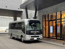 Um ônibus Novotel NARA HINO estacionado em frente a um edifício com fachada moderna e grandes janelas.