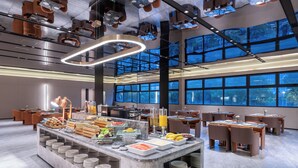 Uma área de café da manhã moderna com ilha central, diversas opções de assento e janelas amplas que oferecem iluminação natural.