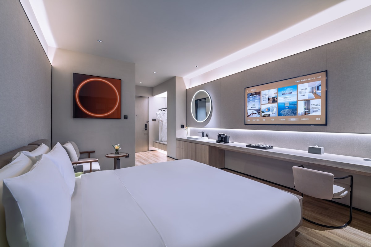 Quarto de hotel moderno com uma cama grande, uma escrivaninha e uma TV exibindo os serviços do quarto.