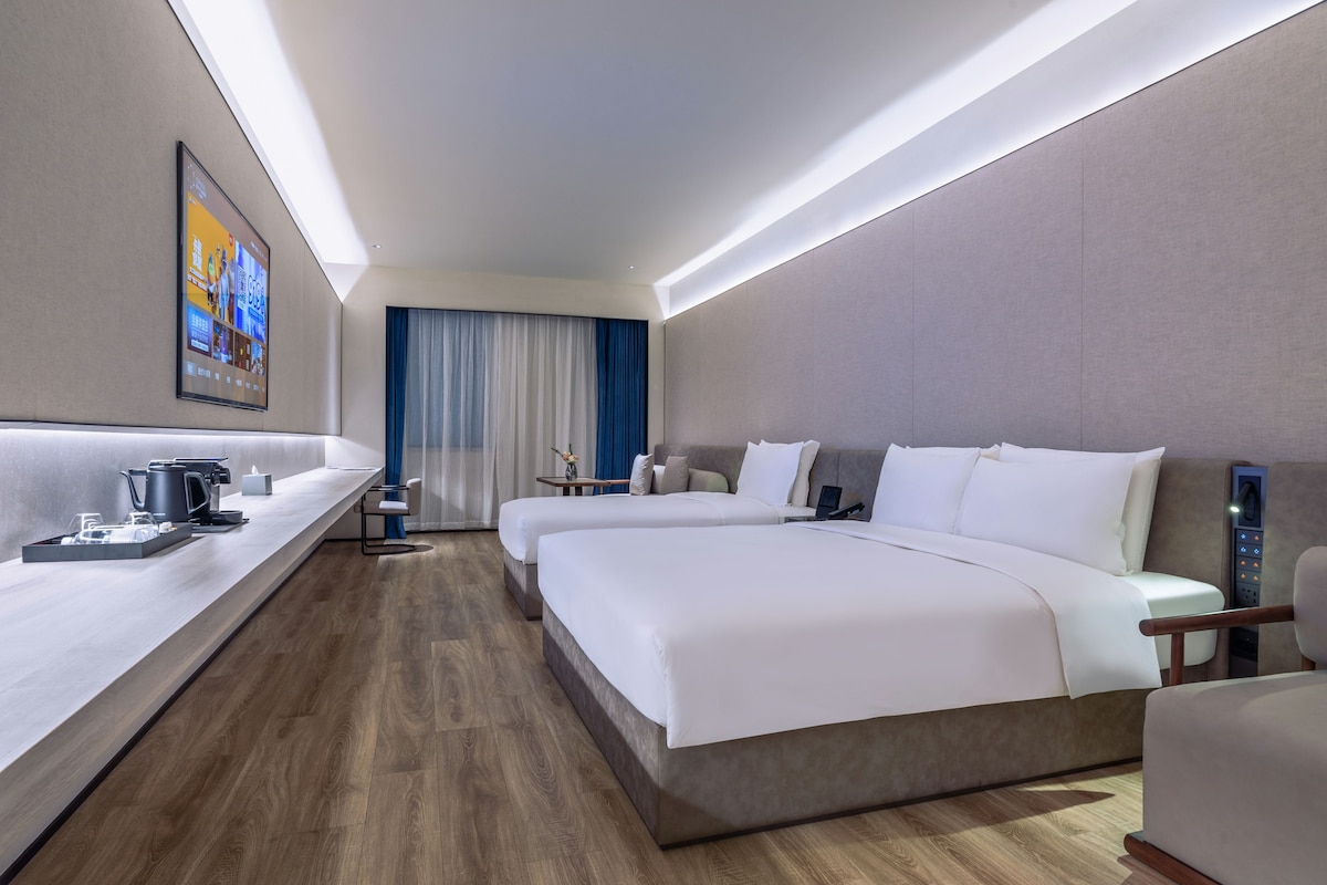Quarto de hotel moderno com uma cama comprida e estreita, área de estar separada, televisão de tela plana e um espaço para café.