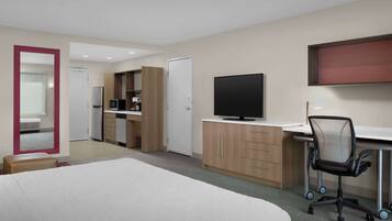 Quarto de hotel com cama, escrivaninha, cadeira, televisão e cozinha compacta.