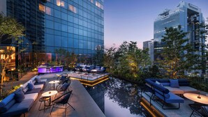 Um bar na cobertura ao ar livre, com mesas e cadeiras e uma piscina, rodeado por edifícios modernos.