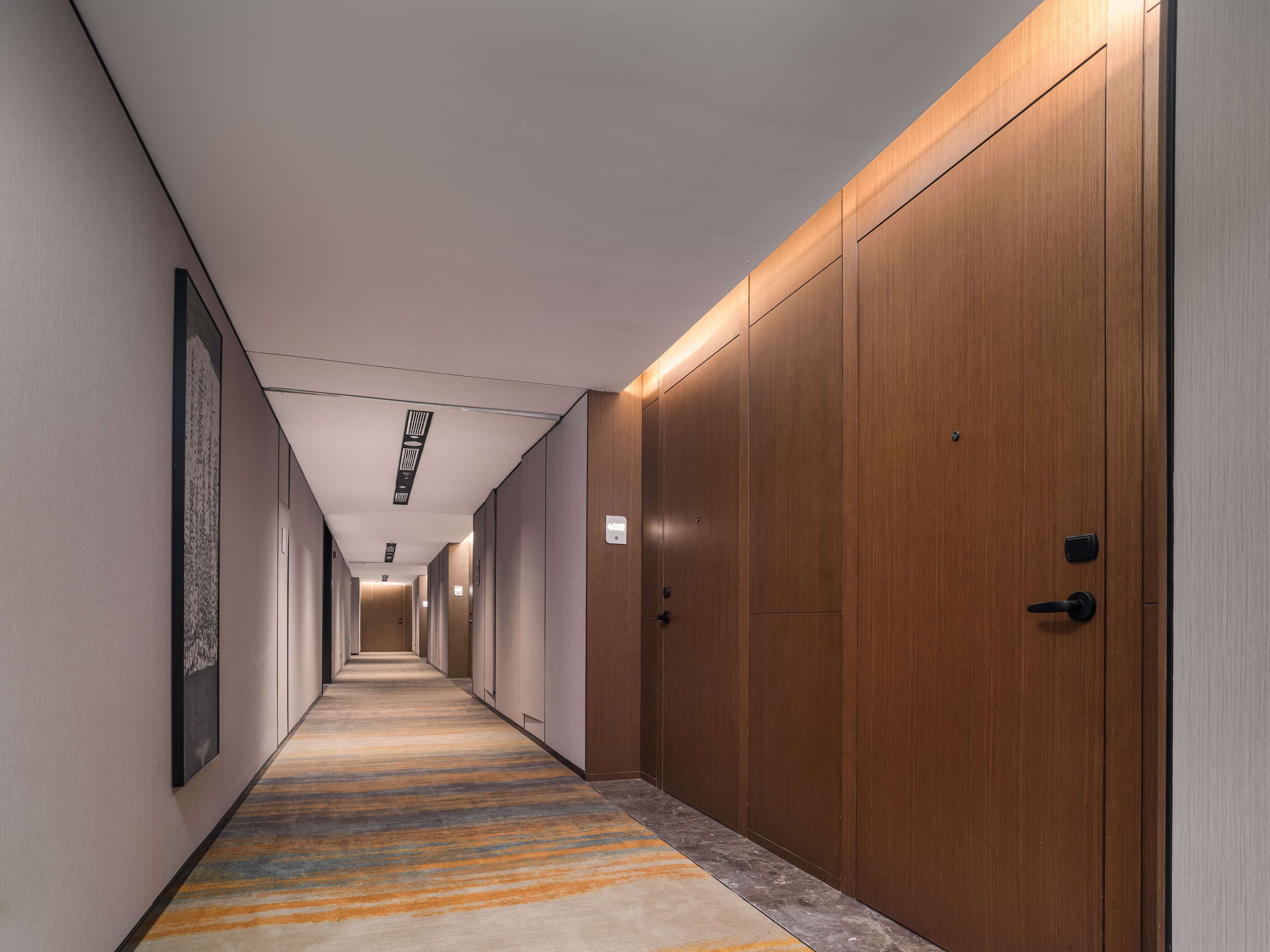 Um corredor moderno de hotel com portas de madeira, carpete estampado e obras de arte emolduradas nas paredes.