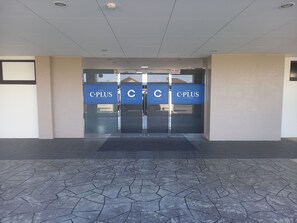 Entrada de um hotel com portas de vidro e uma placa azul que diz "HOTEL C-PLUS".
