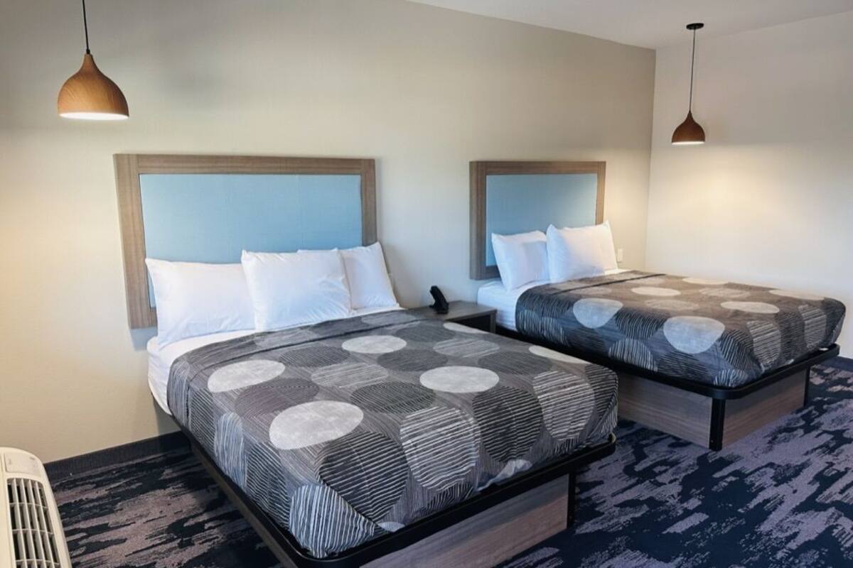Quarto de hotel com duas camas, cada uma com cabeceira e mesa de cabeceira.