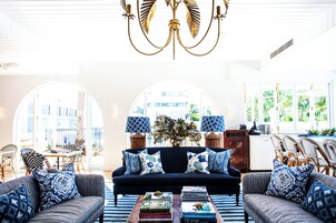 Uma sala de estar com um sofá azul escuro, almofadas estampadas, uma mesa de centro com livros e um candelabro.