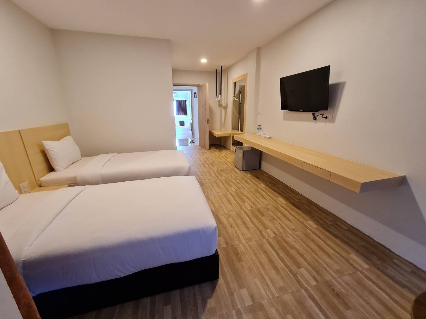 Quarto de hotel com duas camas, televisão presa na parede, chão de madeira e um cesto de lixo pequeno.