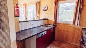 Cozinha compacta com paredes de madeira, chão de azulejos, pia e janela com cortinas.