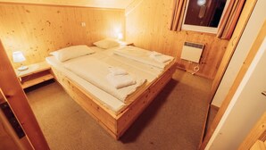 Quarto de madeira com uma cama, mesa de cabeceira, janela e radiador.