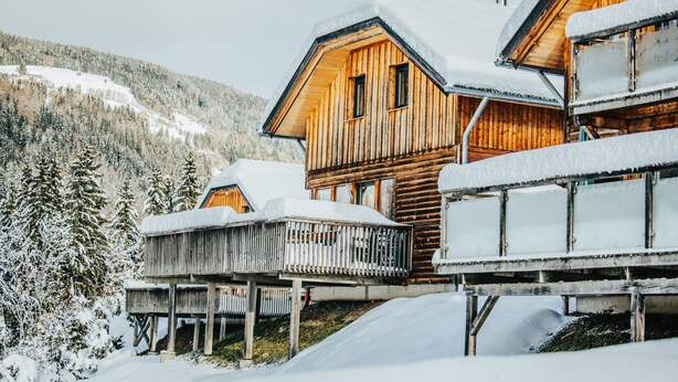 Uma chalé de madeira com varanda e vista para montanhas cobertas de neve.