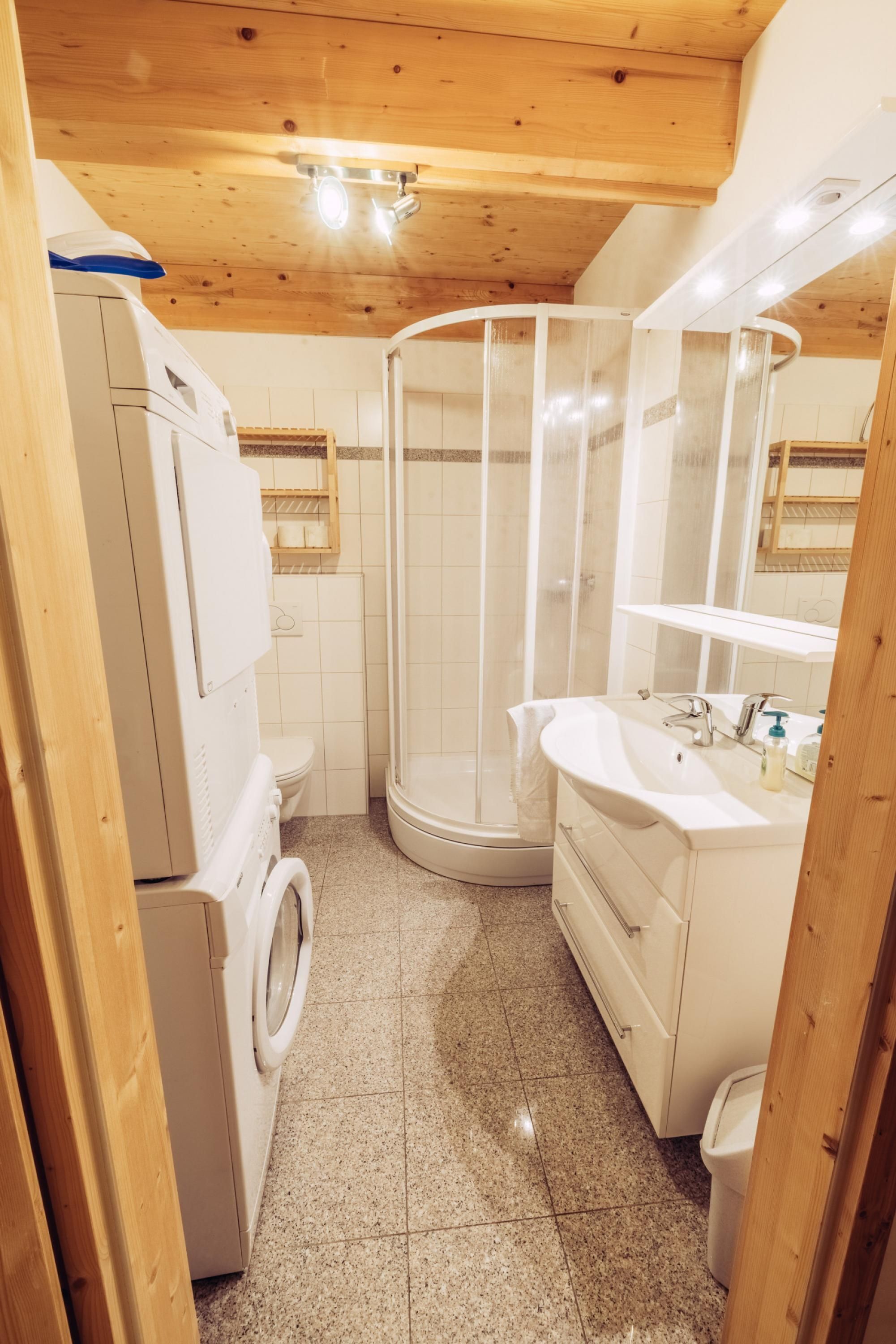 Casa de banho compacta com máquina de lavar, cabine de duche e lavatório com espelho.