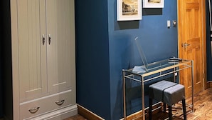 Quarto com parede azul, porta de madeira, armário com gavetas e uma pequena mesa com um laptop.