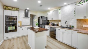 Uma cozinha moderna com armários brancos, uma ilha central, eletrodomésticos de aço inoxidável e bancada de mármore.