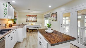 Uma cozinha moderna com armários brancos, bancada de madeira e um espaço de refeições com mesa e cadeiras.