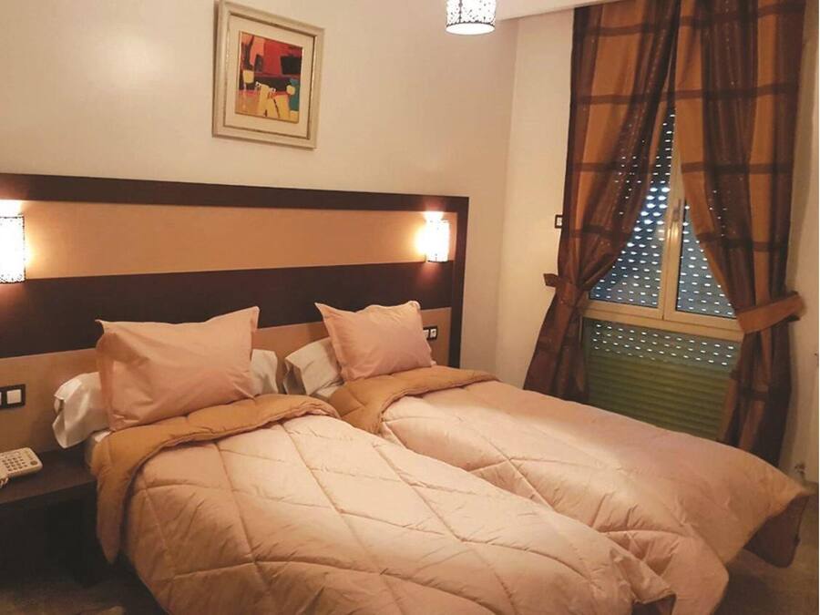 Uma cama de casal com edredom acolchoado, abajures, um telefone e uma janela com cortinas.