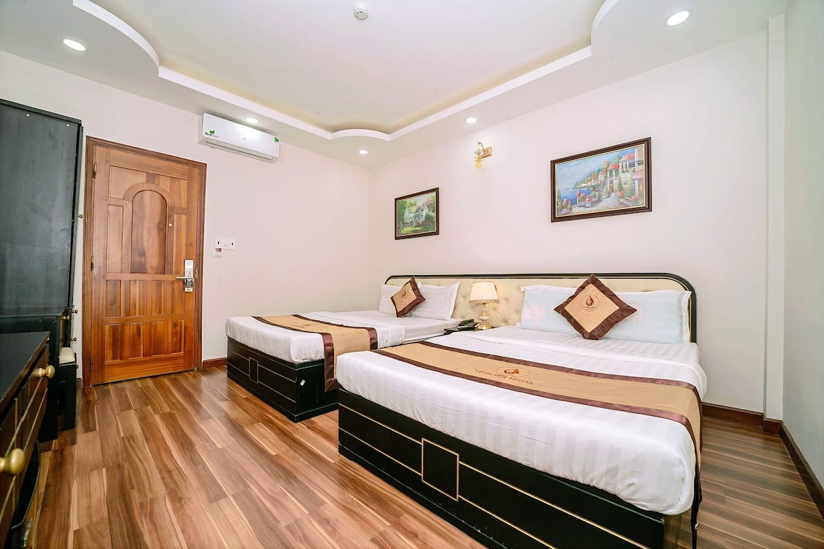 Quarto de hotel com duas camas, piso de madeira, televisão e uma porta.