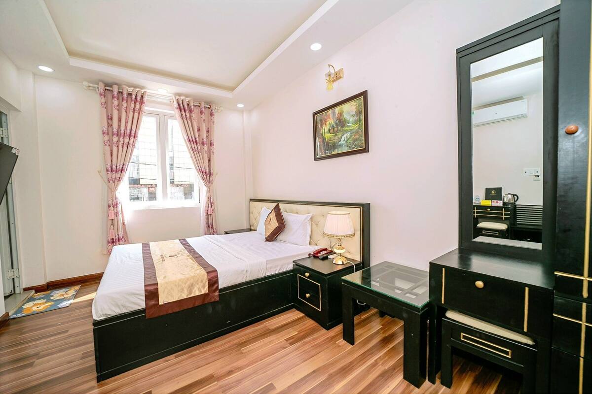 Quarto de hotel com cama, mesa de cabeceira, abajur, cômoda e uma pintura na parede.
