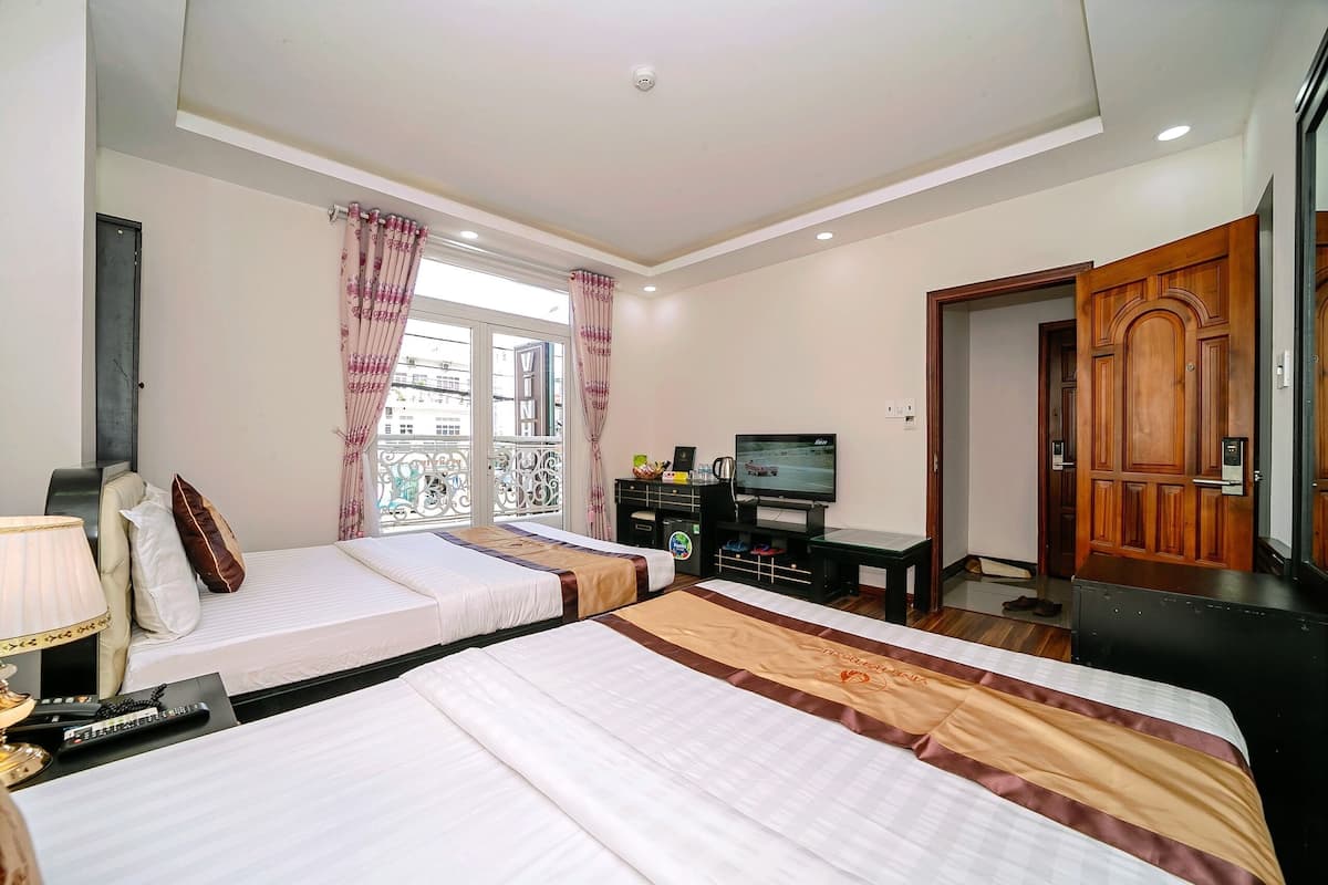 Quarto de hotel com duas camas, televisão, secretária com computador e janela com cortinas.