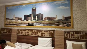 Quarto de hotel com uma grande fotografia emoldurada de um horizonte urbano, uma cama com roupa de cama branca e uma cabeceira decorativa.